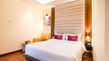 Quarto de hotel com uma cama grande, uma mesinha de cabeceira, uma cadeira e uma luminária fixada na parede.