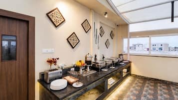 Espaço de café da manhã de hotel com balcão de mármore, itens decorativos fixados na parede e vista através de amplas janelas.
