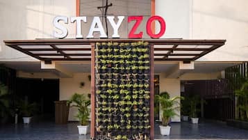 Entrada de hotel com placa indicando 'STAYZO' e um jardim vertical.