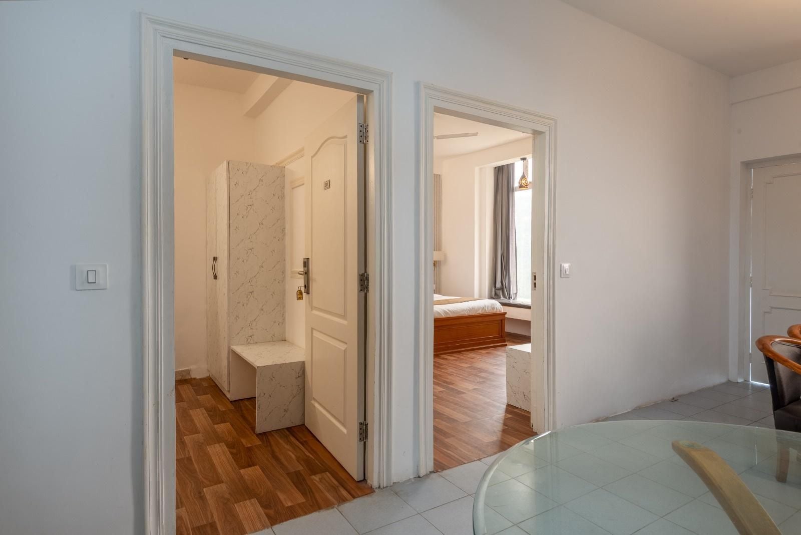 Corredor que dá acesso a um quarto com cama e janela, um banheiro com chuveiro e uma sala de jantar com mesa de vidro.