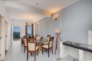 Uma sala de jantar com mesa de vidro e cadeiras de madeira, luminária de chão e vista para o exterior.