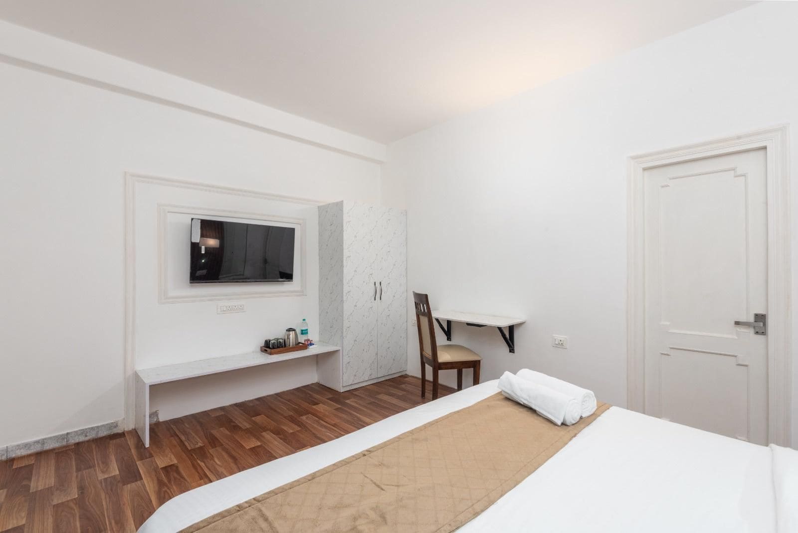 Quarto de hotel com cama, escrivaninha, cadeira, guarda-roupa e janela.