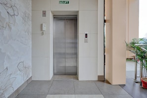 Um elevador com um visor digital, uma placa de elevador acima e uma parede com desenhos abstratos de linhas.