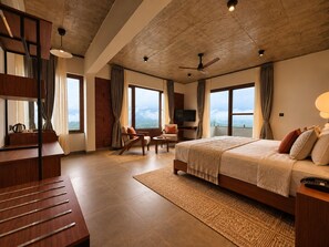 Quarto de hotel com cama grande, escrivaninha, cadeira, televisão e varanda com vista.