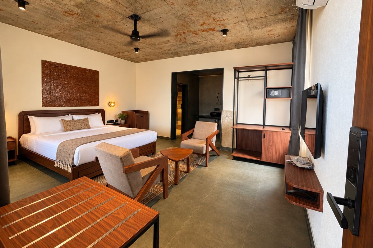 Quarto de hotel com cama, escrivaninha, cadeira, televisão e ventoinha no teto.