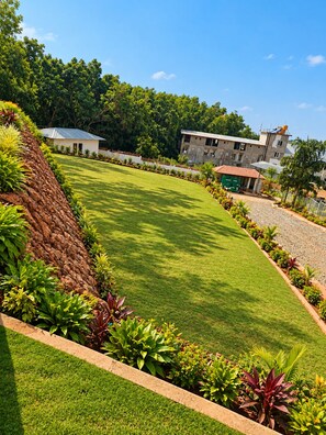 Um jardim ajardinado com gramado, uma parede de contenção de pedra e um edifício com várias janelas e telhado plano.