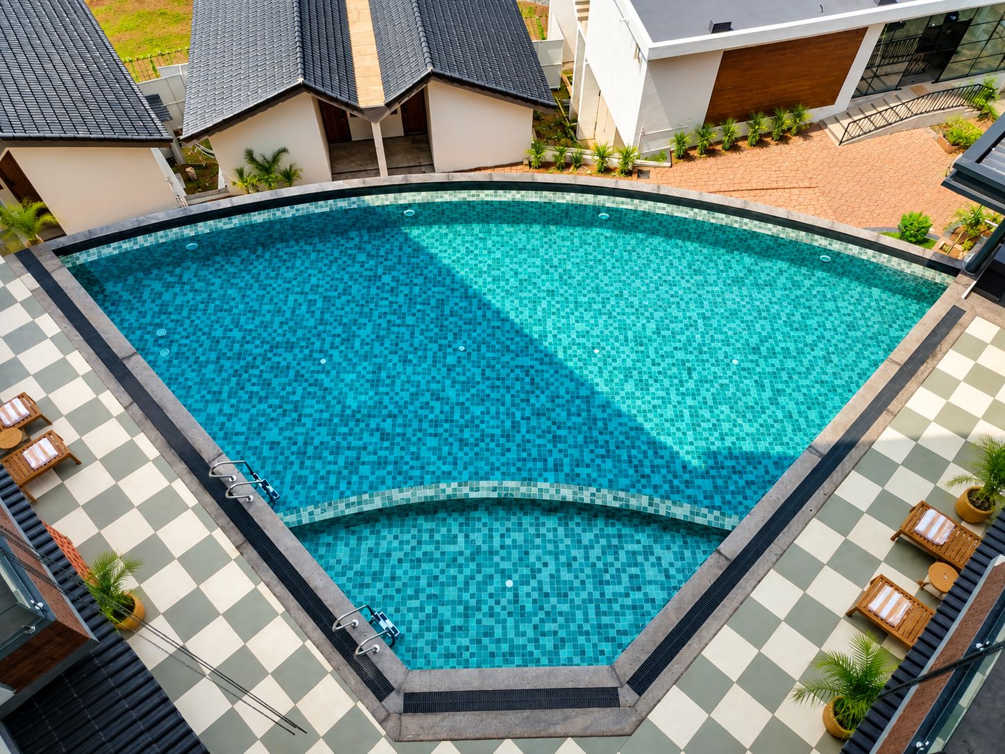 Piscina com deck quadriculado e espreguiçadeiras, cercada por edifícios.