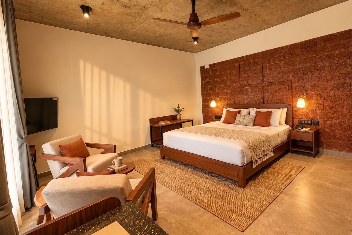 Quarto de hotel moderno com uma cama grande, televisão de tela plana, cabeceira de madeira e parede de destaque em tijolo.
