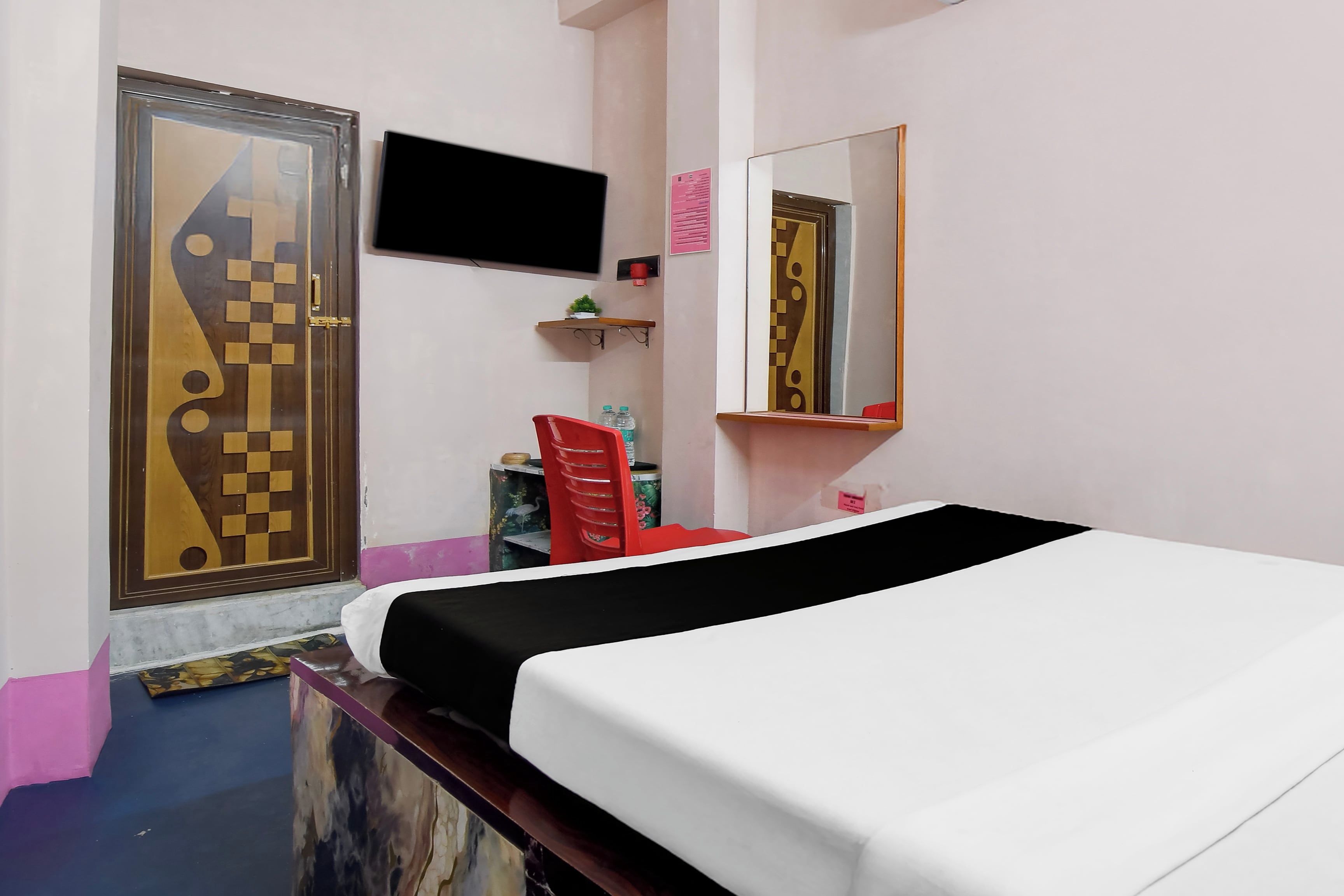 Quarto de hotel com cama, escrivaninha, cadeira, televisão e espelho.