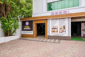 Edifício Pearl Residency com calçada quadriculada na frente, uma placa com comodidades e uma grande janela sobre a entrada.
