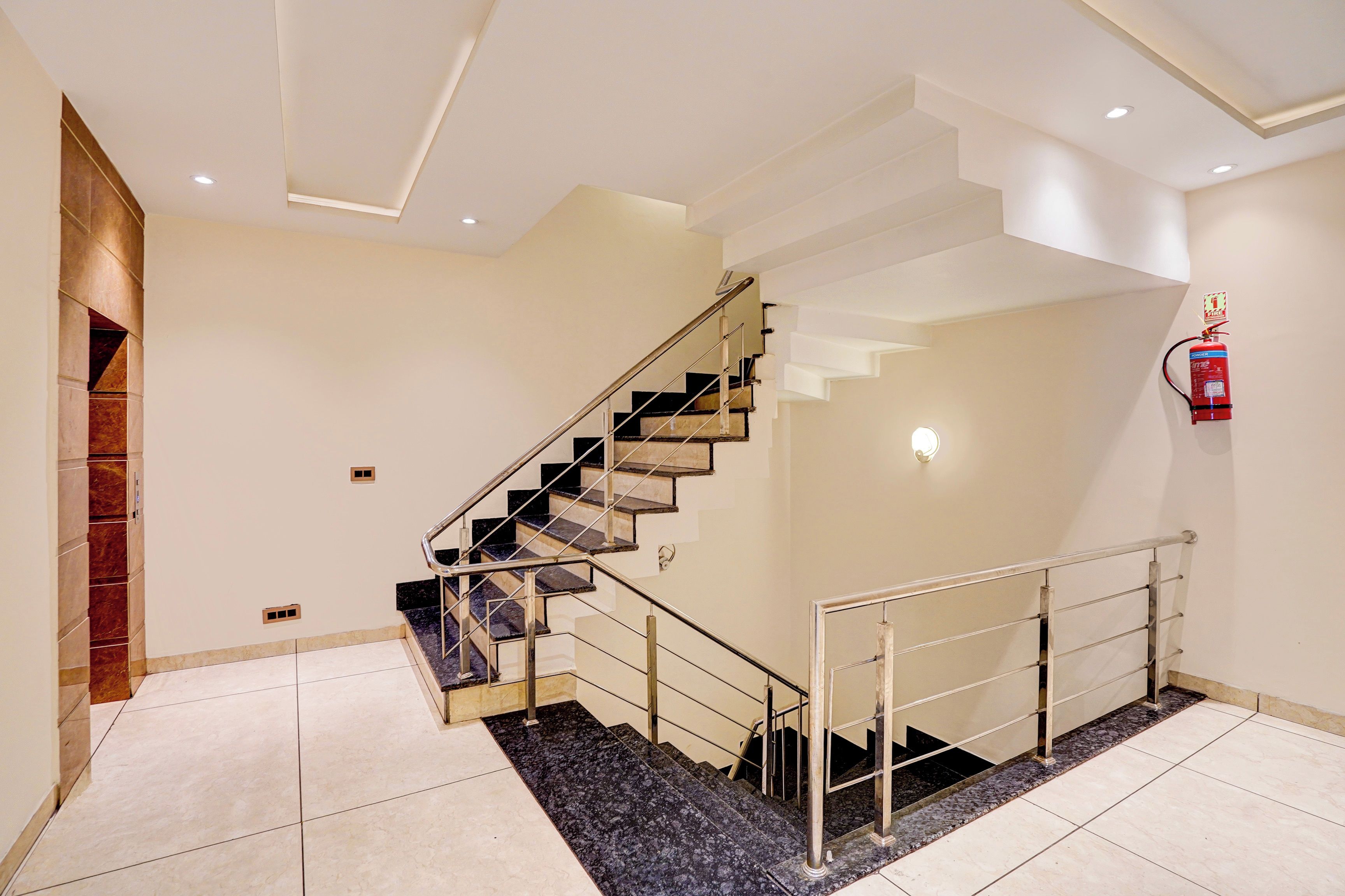 Escadaria moderna com corrimão de metal e extintor fixado na parede, além de piso revestido com azulejos.