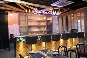 Uma área de bar com uma placa de neon, banquetas e prateleiras com copos.