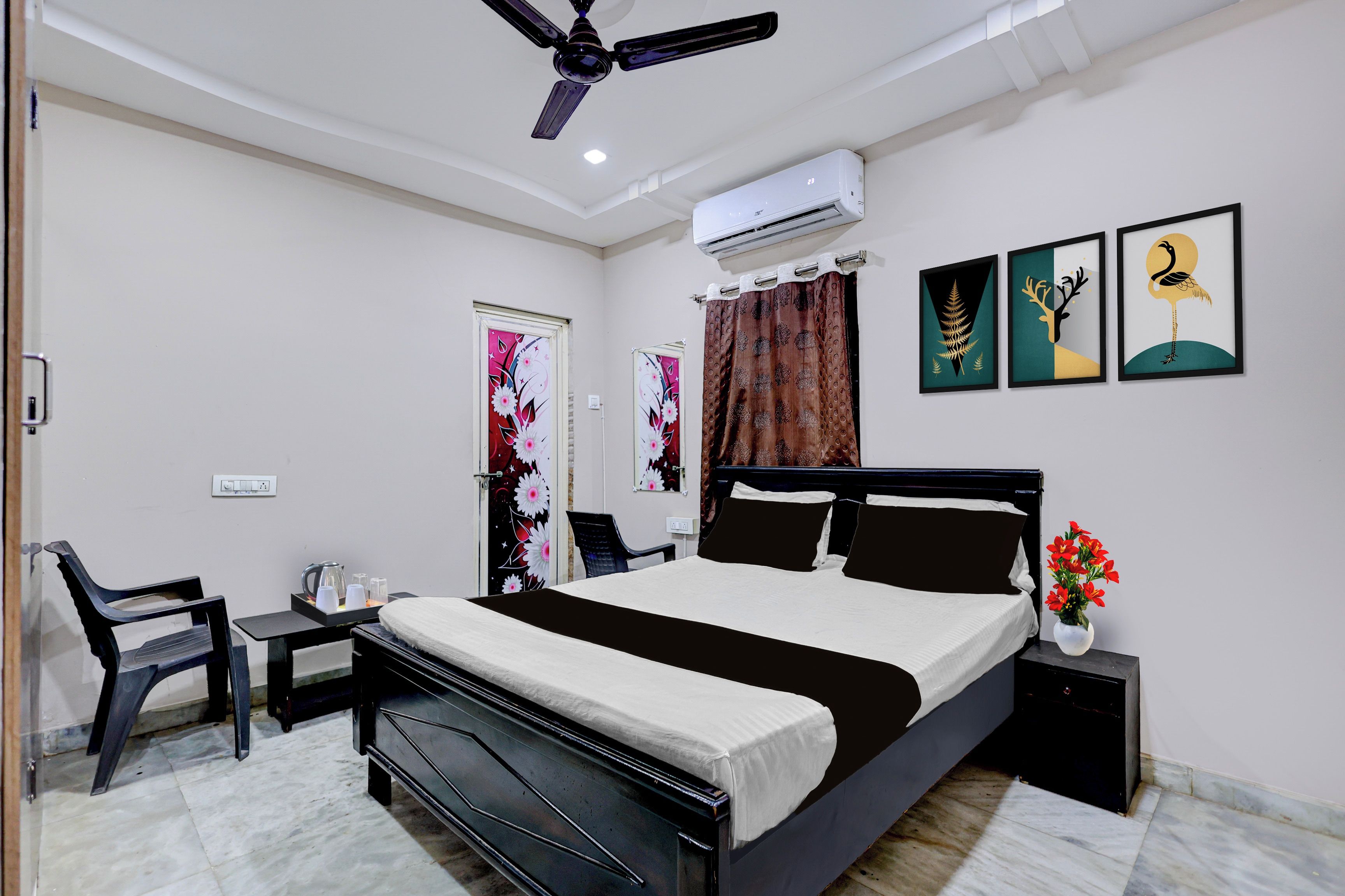 Quarto de hotel com cama, escrivaninha, cadeira, aparelho de ar condicionado e obras de arte na parede.