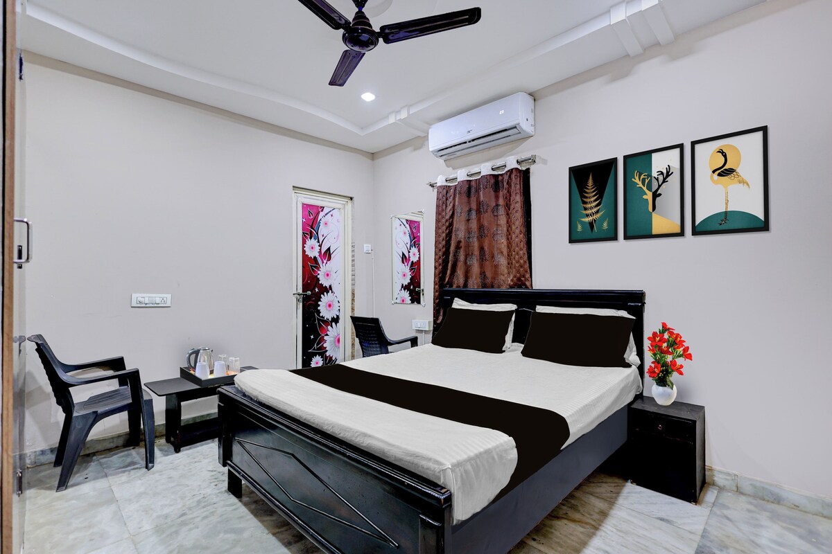 Quarto de hotel com cama, escrivaninha, cadeira, aparelho de ar condicionado e obras de arte na parede.