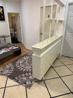 Quarto com cama, uma mesinha, tapete estampado e um banco branco.