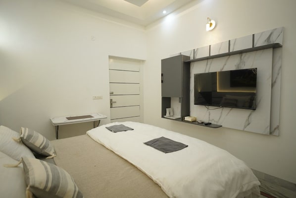 Quarto moderno com cama, mesas de cabeceira, televisão embutida e guarda-roupa.