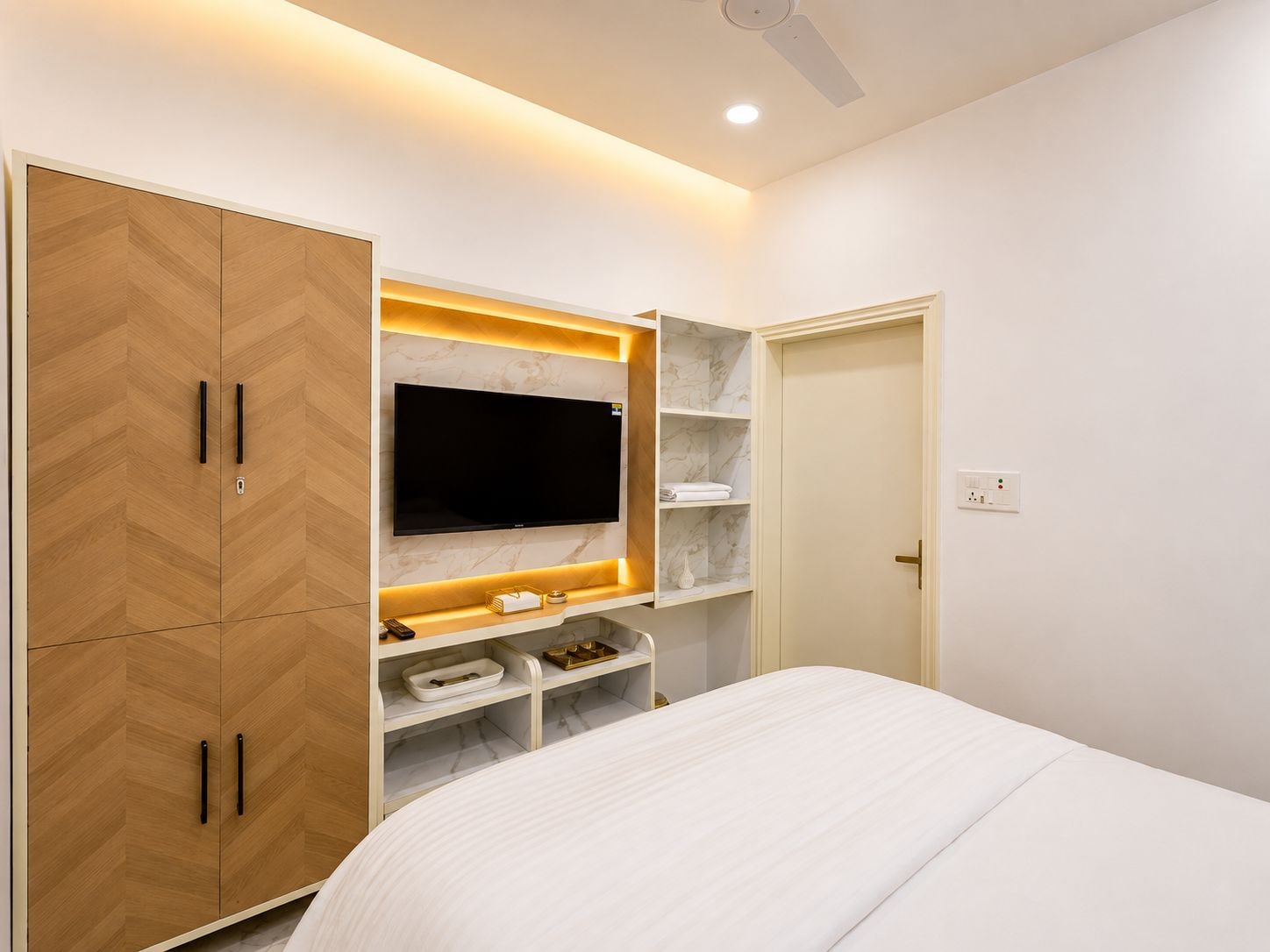 Quarto com cama, televisão montada em um armário de madeira e porta com interruptor de luz.