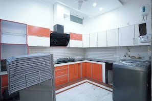 Cozinha compacta com eletrodomésticos modernos, armários em branco e laranja e painel de azulejos.