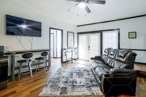Uma sala de estar moderna com televisão de tela plana, sofá de couro, área de jantar com cadeiras e ventilador de teto.