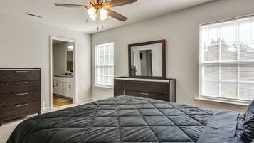 Quarto com cama, cômoda, espelho, ventilador de teto e janela com persianas.