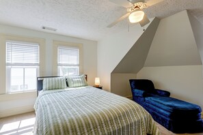 Quarto com cama, duas janelas, ventilador de teto e uma cadeira azul.