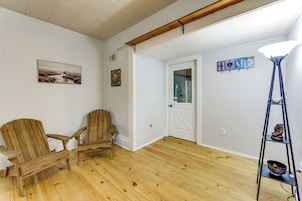 Quarto com piso de madeira, uma cadeira de madeira, uma mesa pequena, um abajur e uma prateleira fixada na parede com um objeto decorativo.