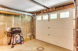 Garagem com piso de concreto, bancada de madeira, churrasqueira e materiais de limpeza.