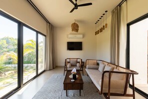Uma sala de estar ampla com uma janela grande, ventilador de teto, televisão de tela plana e área de jantar com mesa e cadeiras.