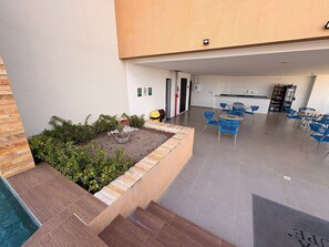 Área de estar moderna ao ar livre com cadeiras azuis e um pequeno jardim com plantas e um elemento decorativo.