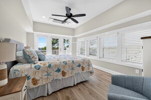 Quarto com cama, ventilador de teto, janela com persianas e vista para o exterior.