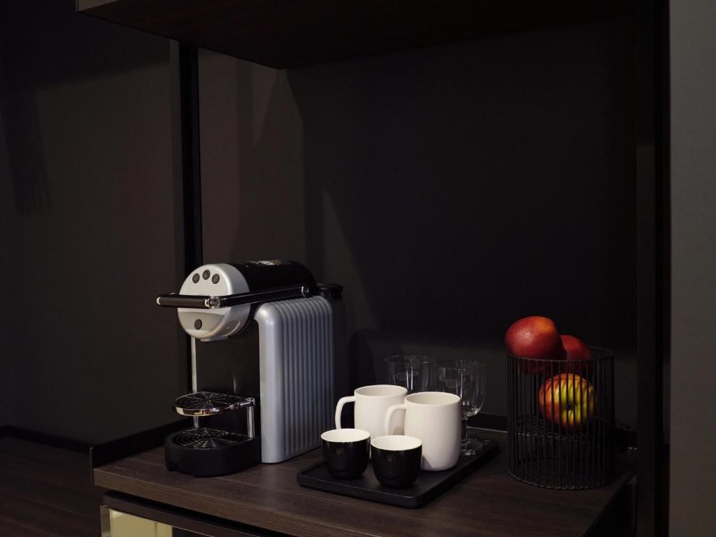 Uma bancada de cozinha com cafeteira, chaleira, cesta de frutas e bandeja com xícaras.