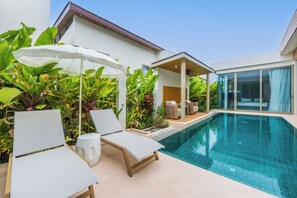 Uma área moderna de piscina ao ar livre com espreguiçadeiras, um espaço coberto para relaxar e vegetação exuberante.