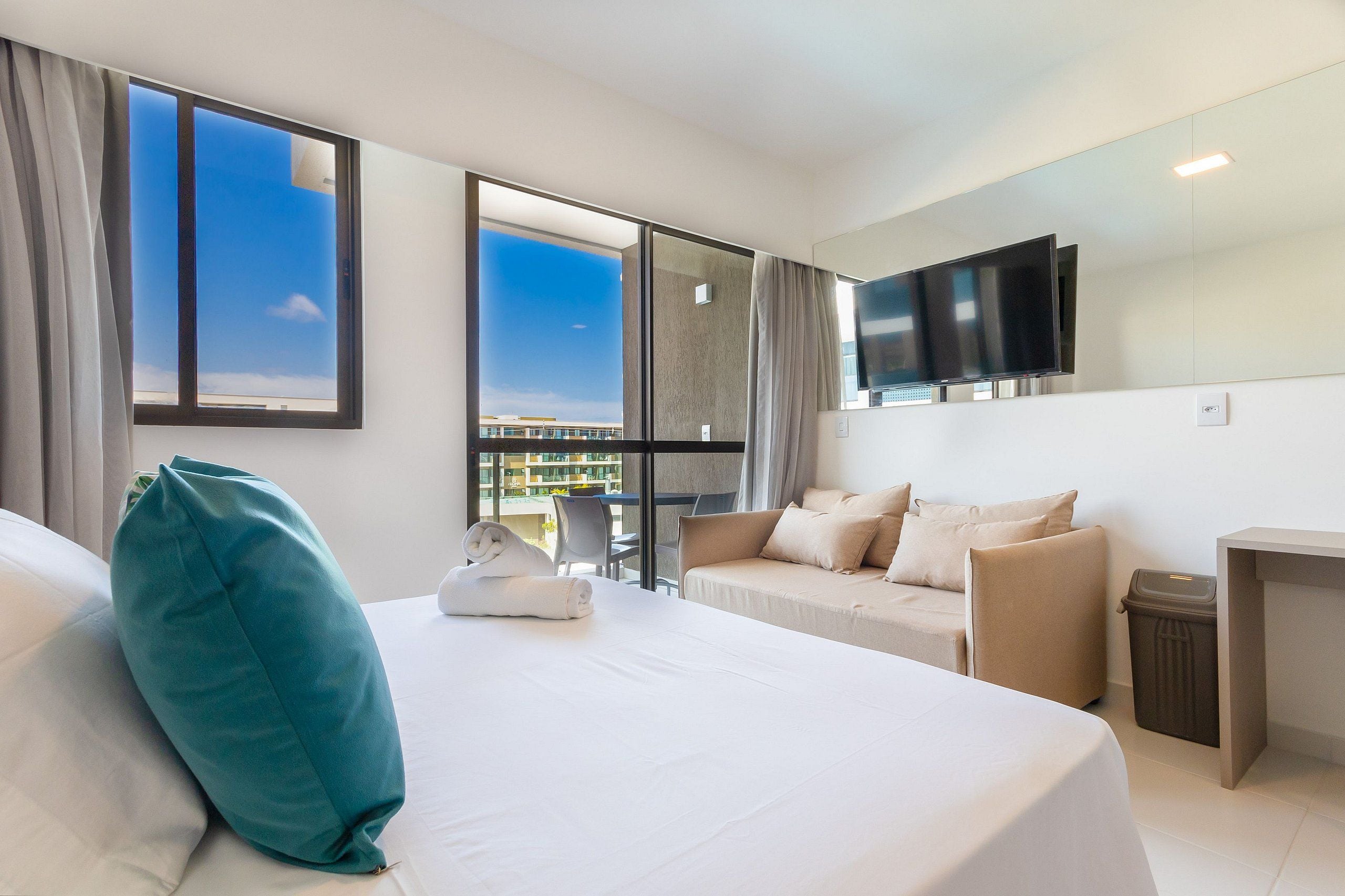 Quarto de hotel com cama, sofá, televisão e vista para a cidade.