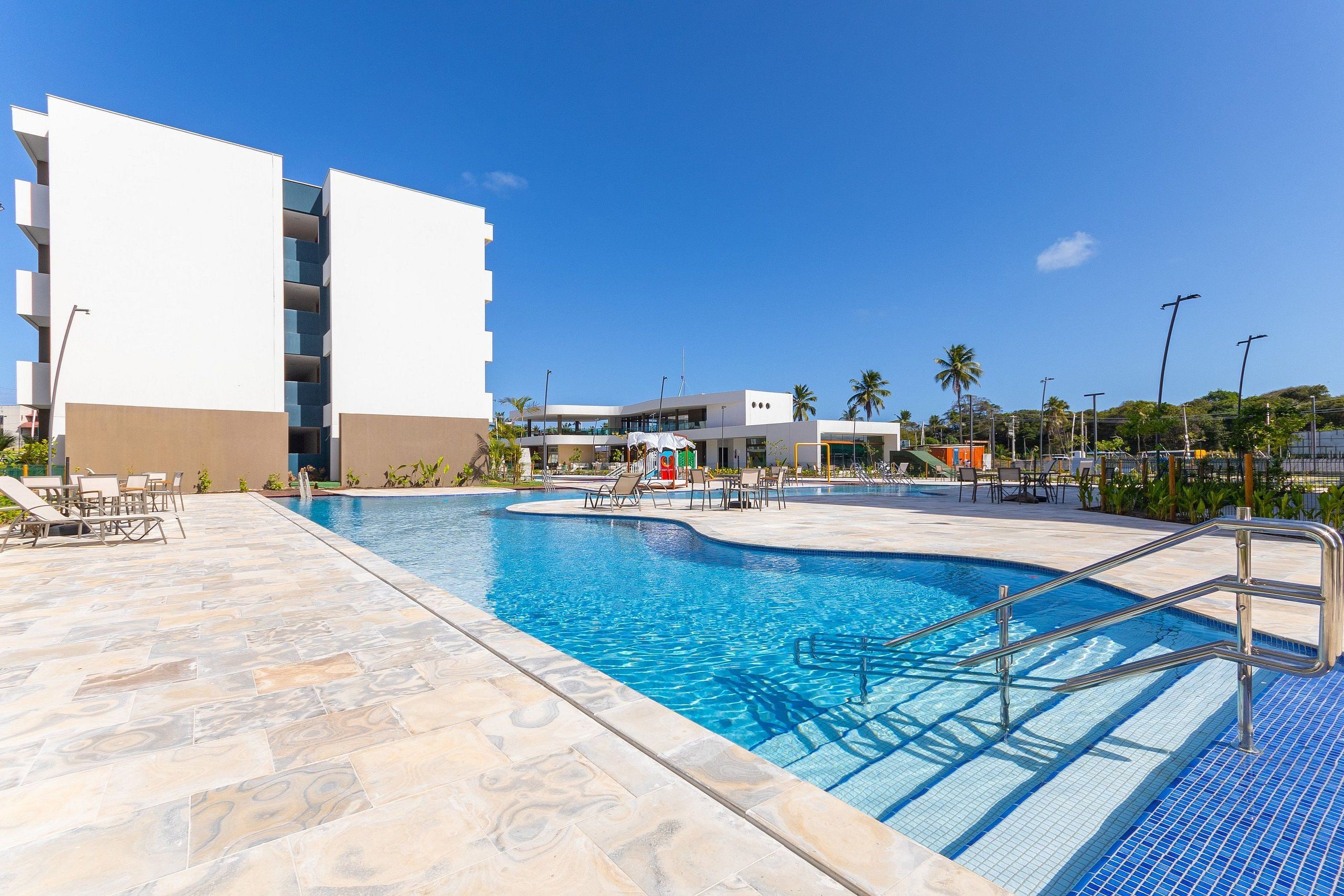 Uma área de piscina com espreguiçadeiras e um edifício com varandas.