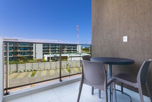 Varanda com mesa e cadeiras, com vista para um estacionamento e um edifício com vários andares.
