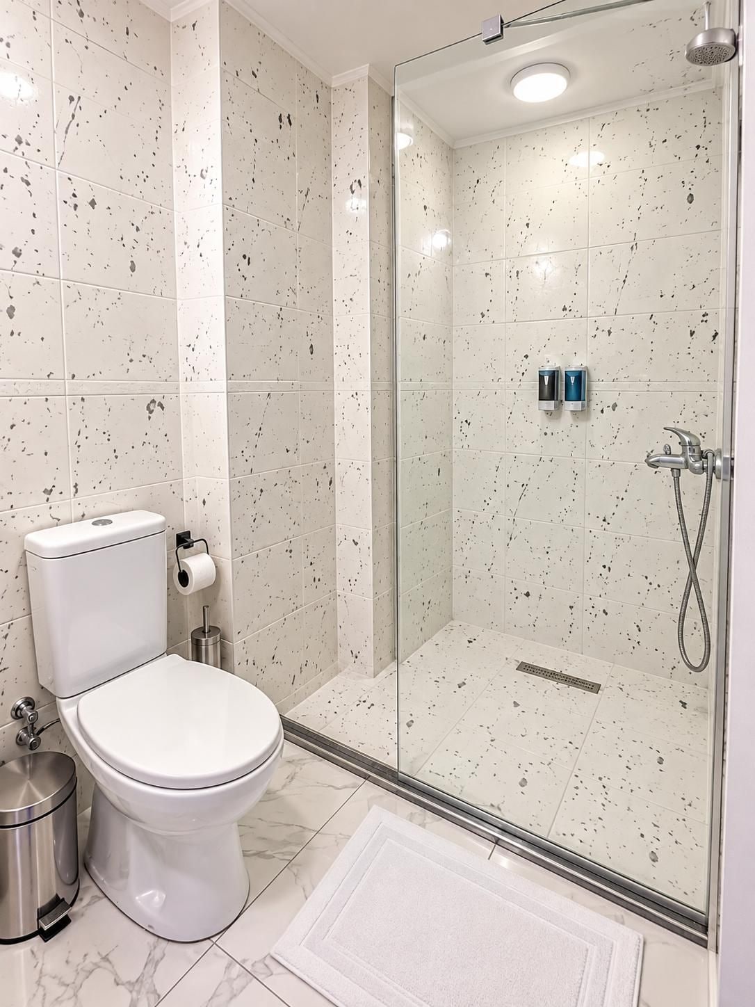Um banheiro moderno com vaso sanitário, chuveiro com box de vidro e piso de mármore.