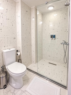 Um banheiro moderno com vaso sanitário, chuveiro com box de vidro e piso de mármore.