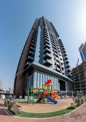 Um edifício moderno com fachada curva e um parquinho infantil na frente.