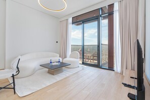 Quarto de hotel moderno com uma janela grande, um sofá, uma mesa de centro e uma TV de tela plana.