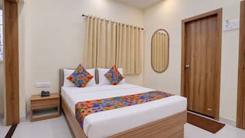 Quarto de hotel com cama, mesa de cabeceira e guarda-roupa de madeira.