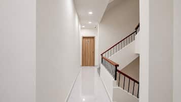 Um interior moderno com um corredor que leva a uma porta de madeira, uma escada com corrimão de madeira e piso revestido de azulejos.