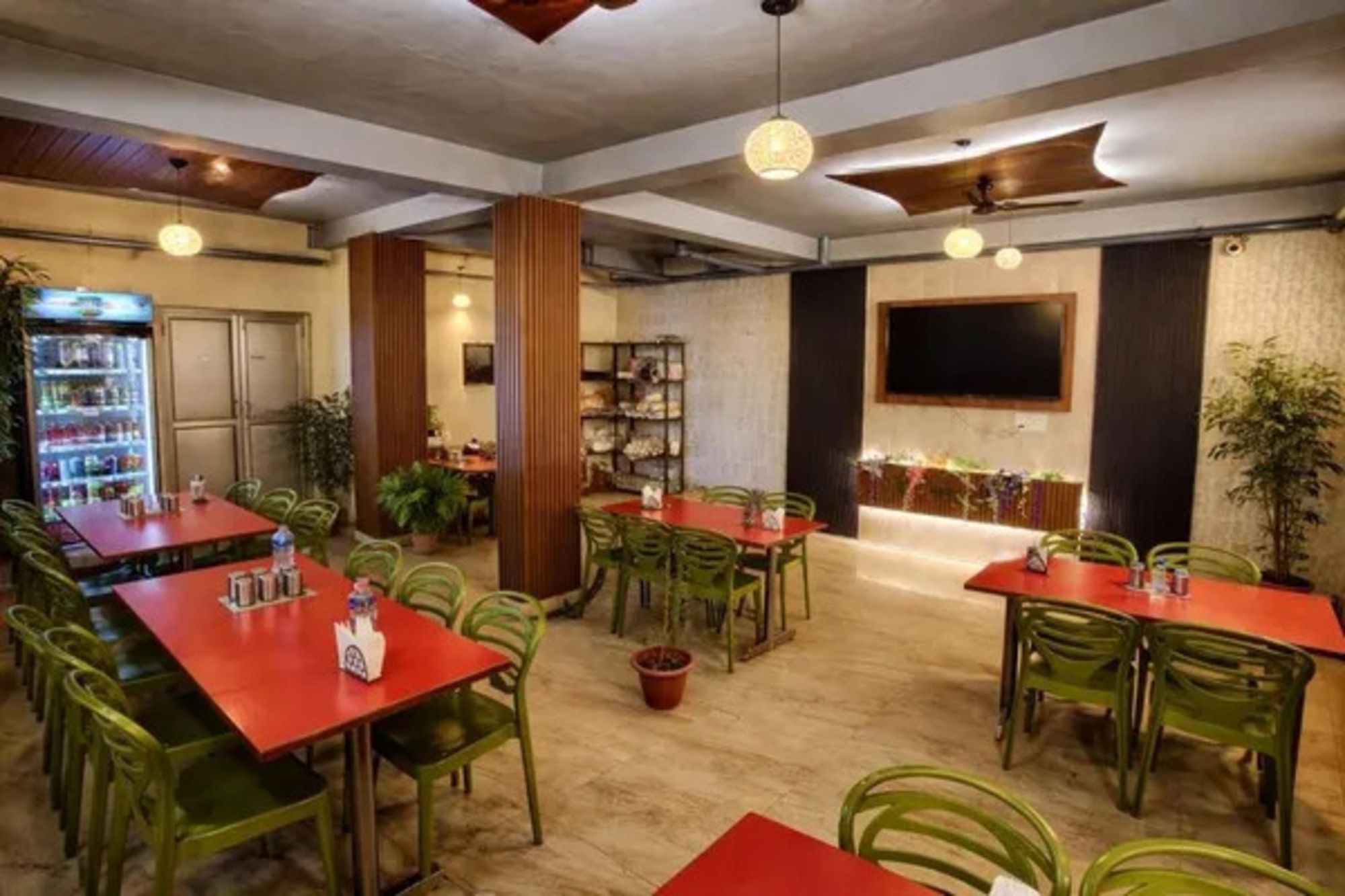 Um restaurante com várias mesas e cadeiras, uma máquina de vendas automática e uma tela de televisão na parede.