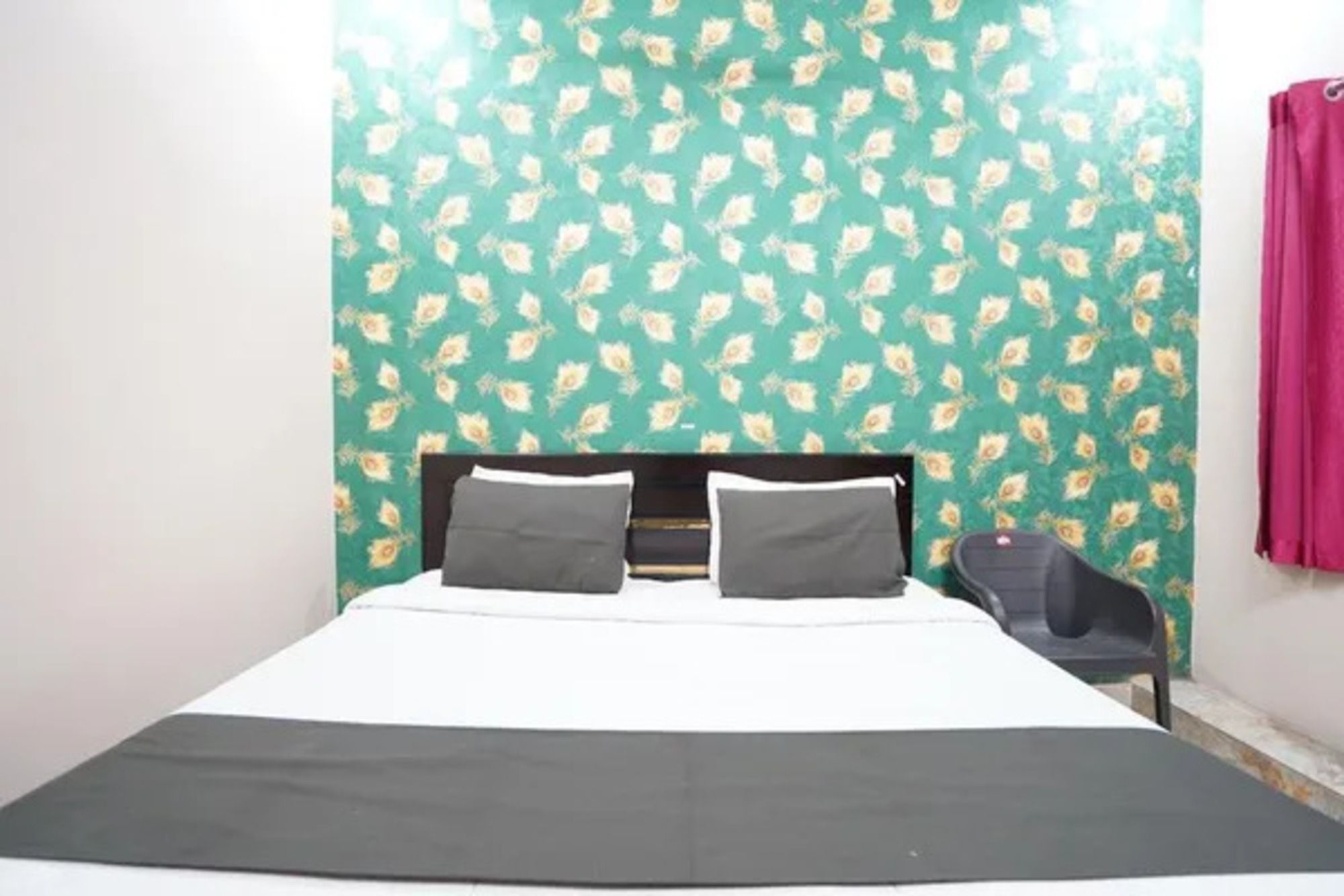 Uma cama com colcha branca e preta, duas almofadas e cabeceira, tudo contra uma parede com padrão floral.