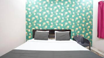 Uma cama com colcha branca e preta, duas almofadas e cabeceira, tudo contra uma parede com padrão floral.
