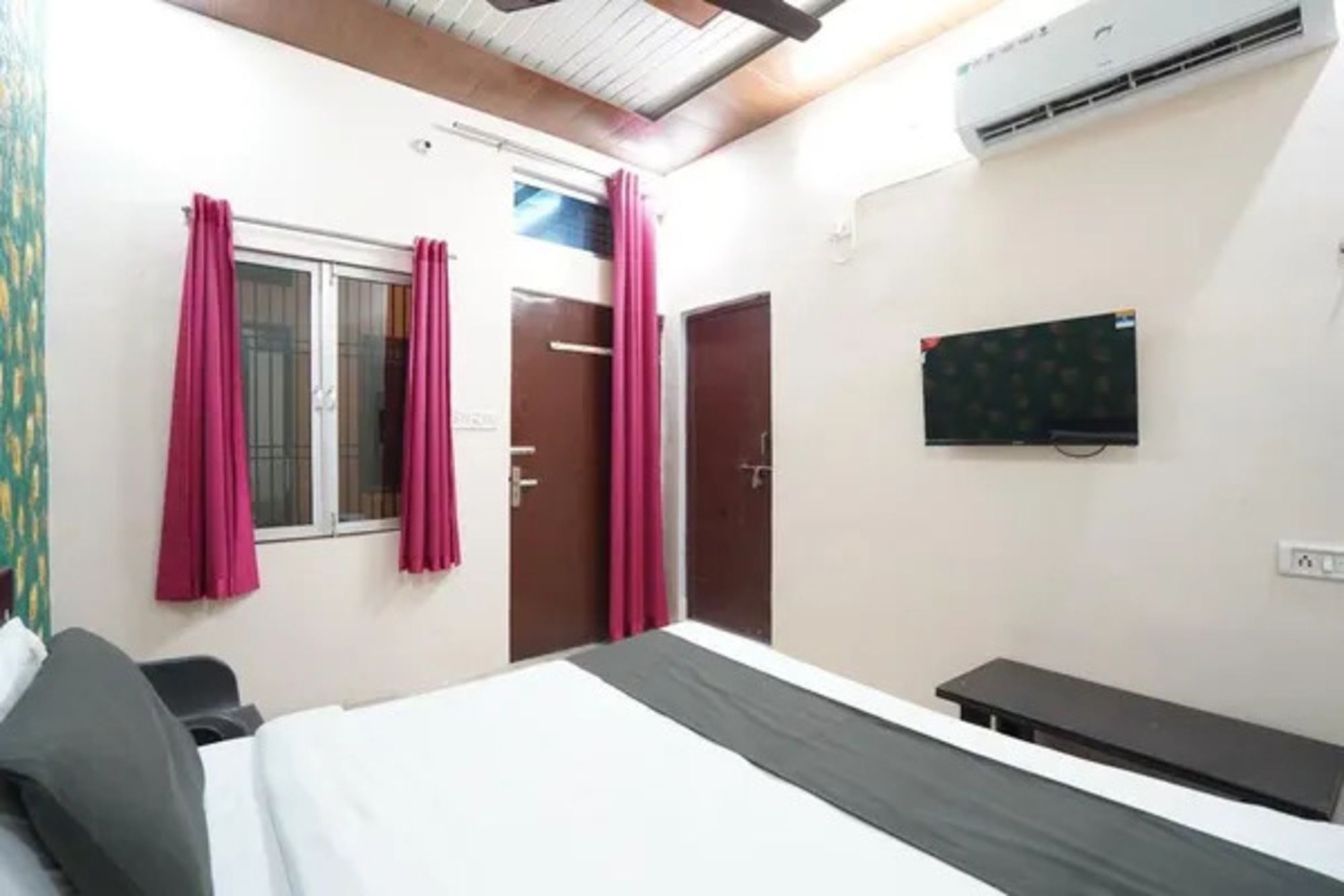 Quarto de hotel com cama, escrivaninha, televisão e janela com cortinas.