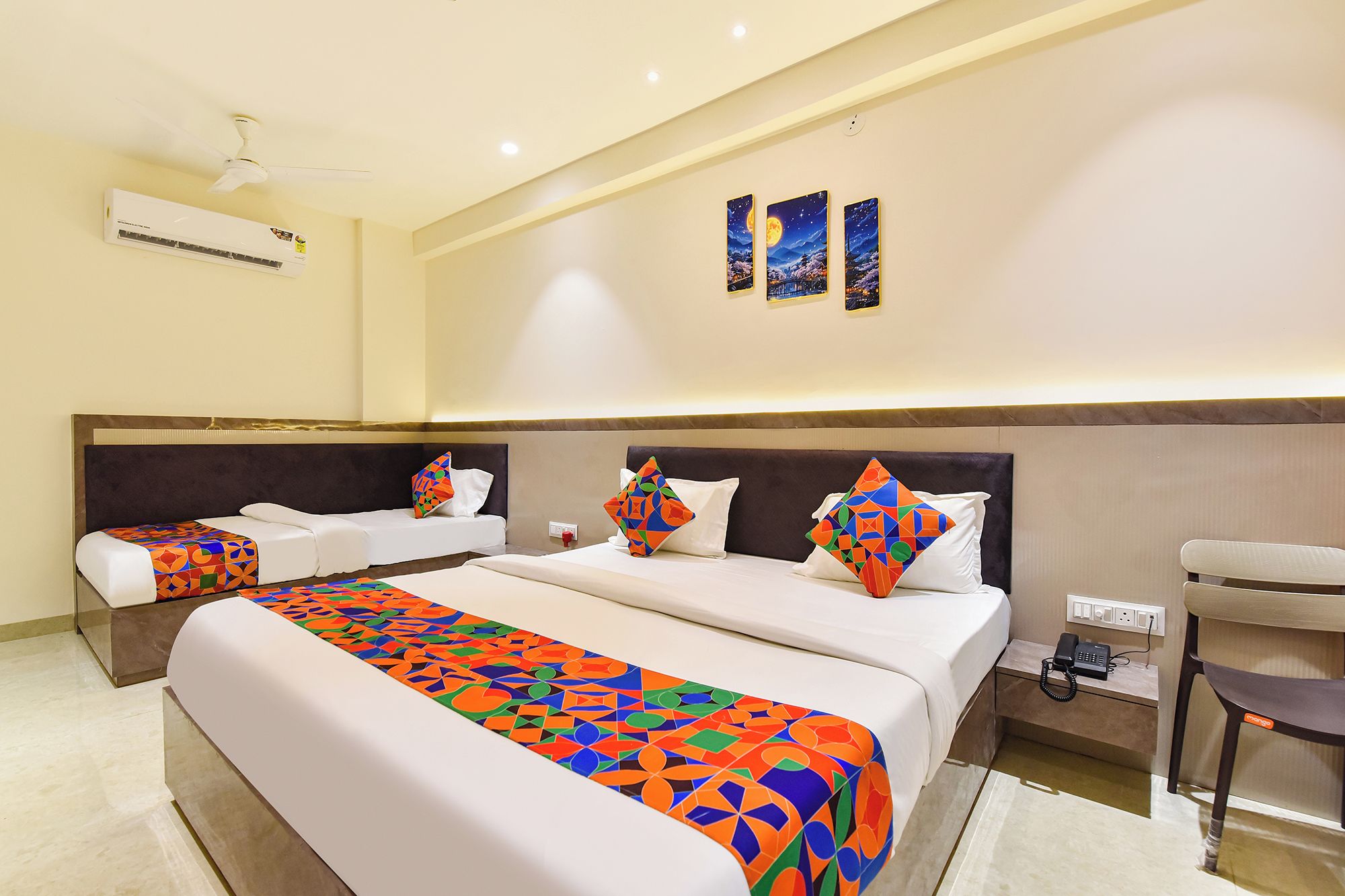 Quarto de hotel com duas camas, ventoinha no teto, aparelho de ar condicionado e uma pintura da noite no muro.