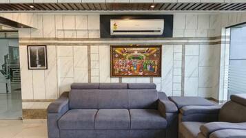 Um hall de entrada com um sofá cinzento, uma pintura emoldurada e um aparelho de ar condicionado no teto.