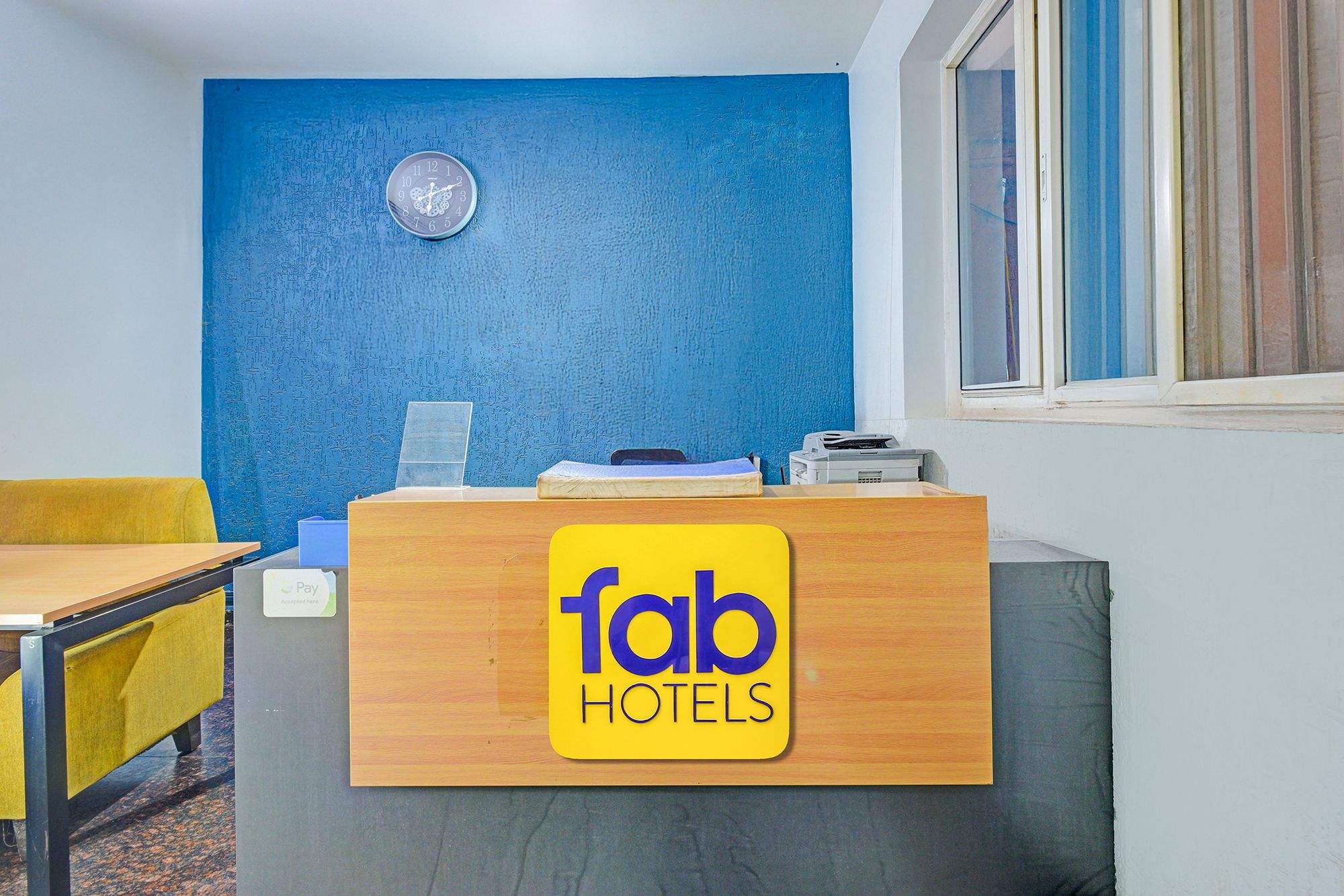 Uma receção com um relógio em cima, uma janela à direita e um letreiro amarelo que diz 'fab HOTELS'.