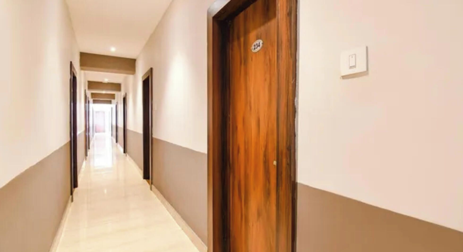 Corredor de hotel com porta de madeira, interruptor de luz e acesso a outro quarto.