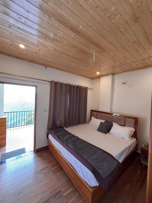 Quarto com teto de madeira, uma cama grande, janela com cortinas e uma varanda.